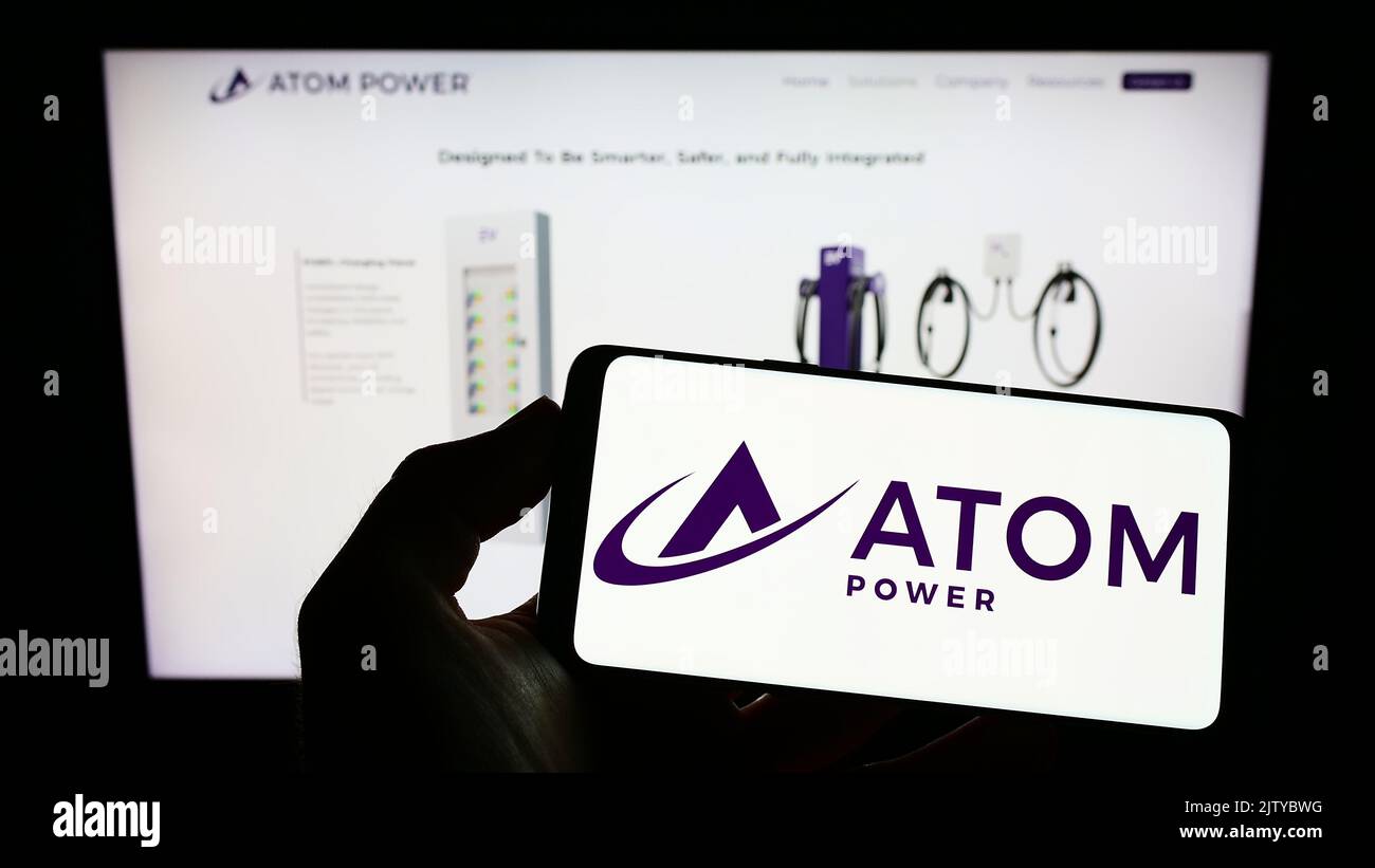 Person holding cellphone with logo of US electric charging company Atom ...