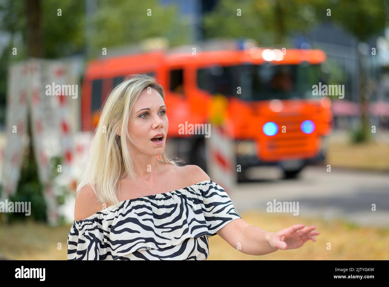 Woman standing in an urban street raising her hand with a shocked or ...