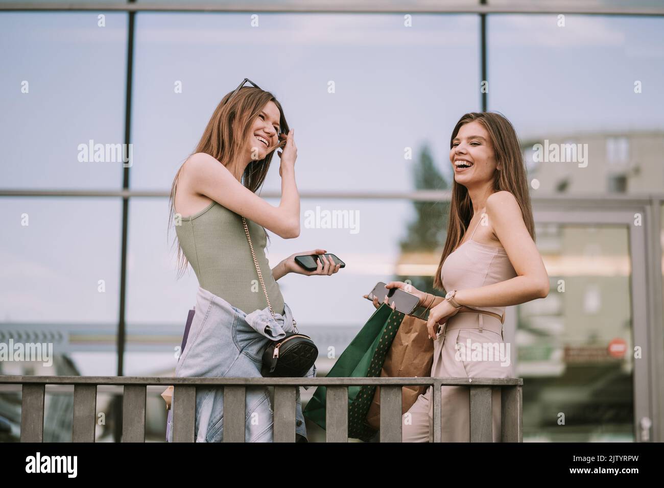 Two pretty girls laughing infront of the mall while holding their ...