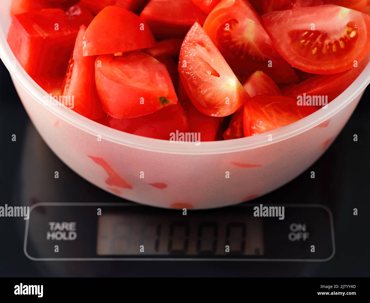 A bowl with a kilogram of tomato slices on a digital scale. Focus is on ...