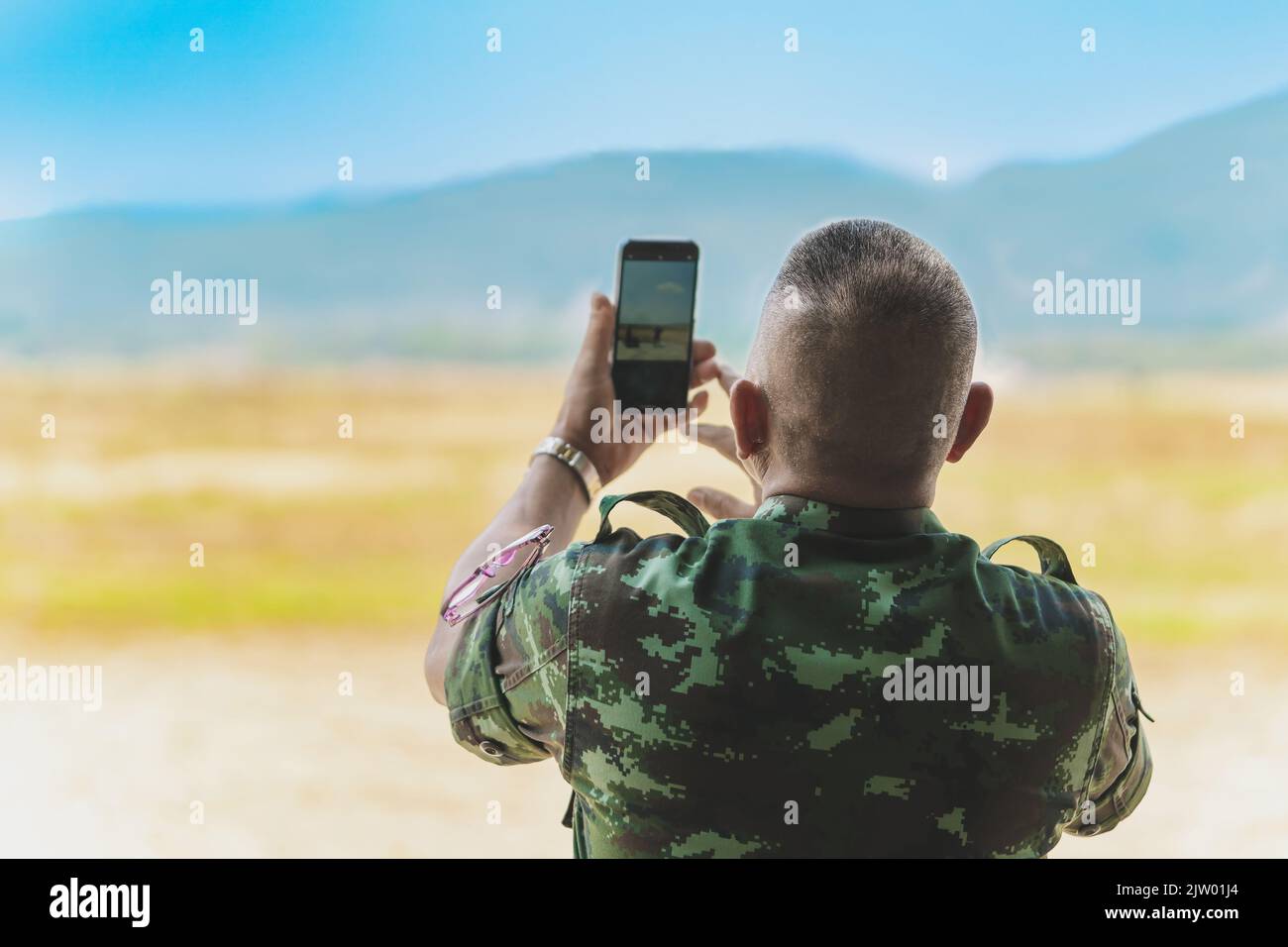 Back view of Asian army soldier using cell phone to take landscape ...