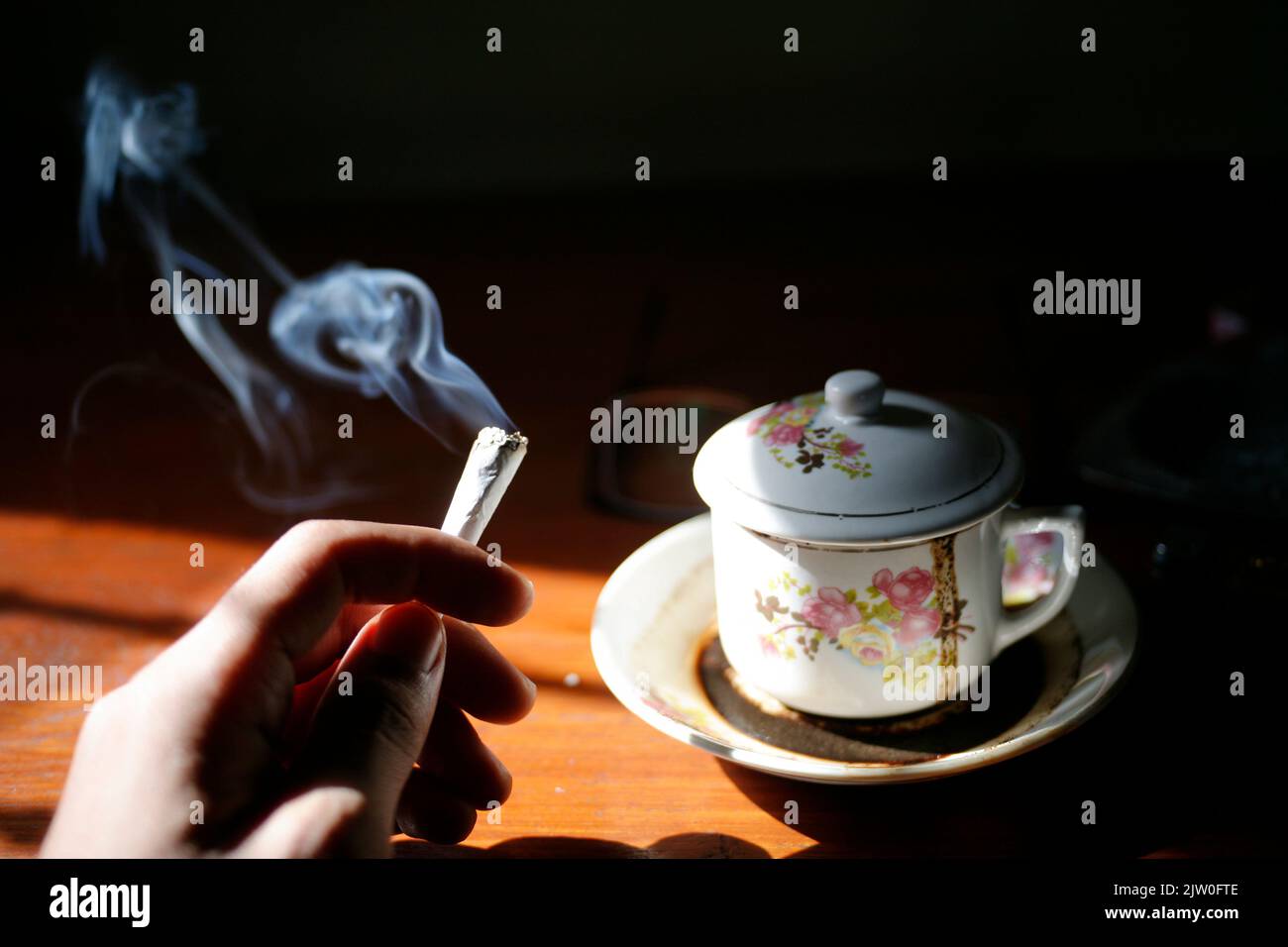Hand holding rolled cigarette with traditional cup of coffee on wooden ...