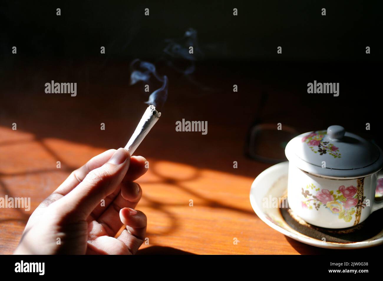 Hand holding rolled cigarette with traditional cup of coffee on wooden ...