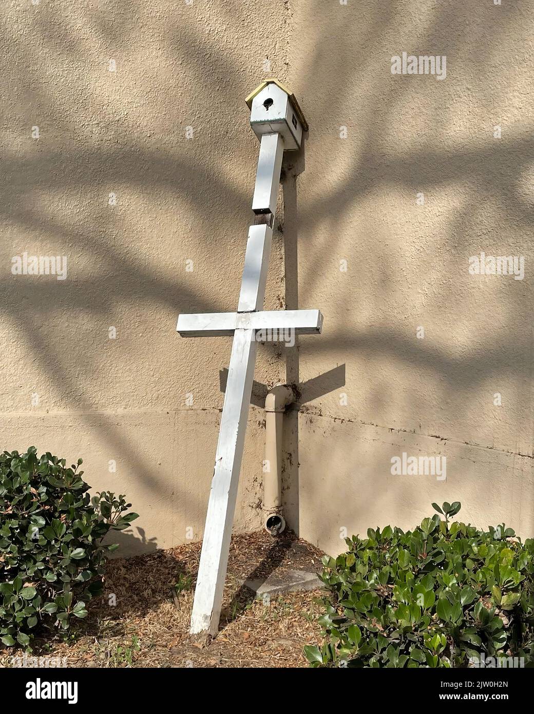 A vertical shot of a wooden white birdhouse with a cross leaning ...