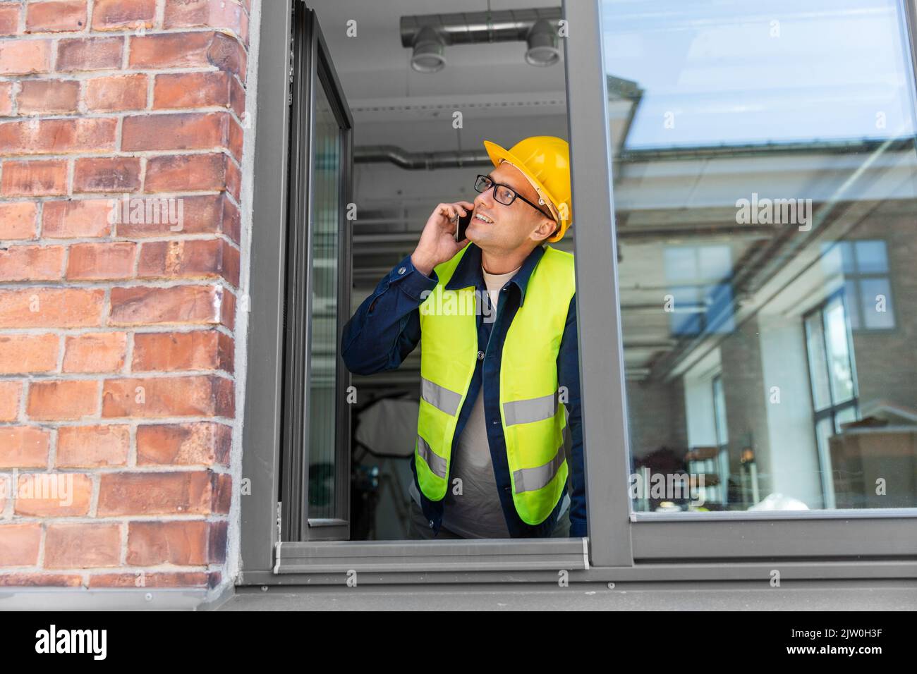 builder looking out window and calling on phone Stock Photo - Alamy