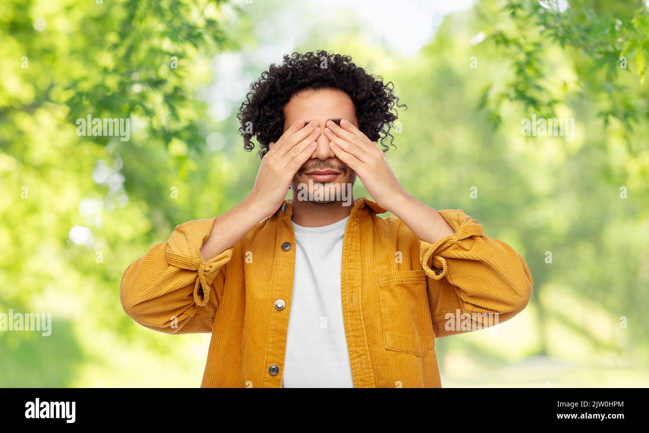 man closing eyes by hands on natural background Stock Photo - Alamy