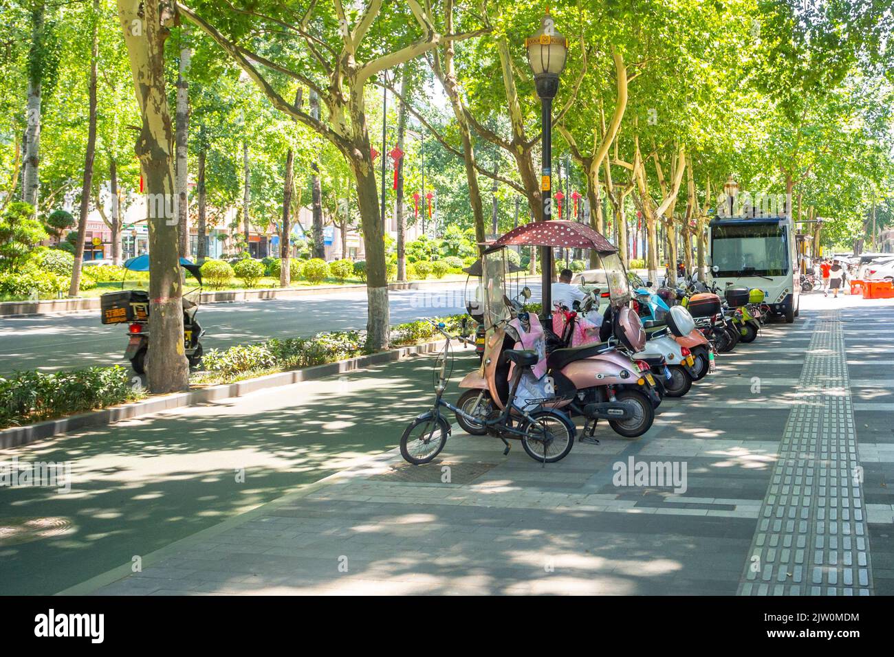 A variety of scooters or cycles are parked on a sidewalk in the ...