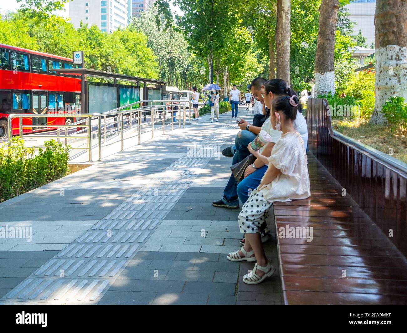 Chinese people sitting in a bench by a sidewalk. A double-decker ...