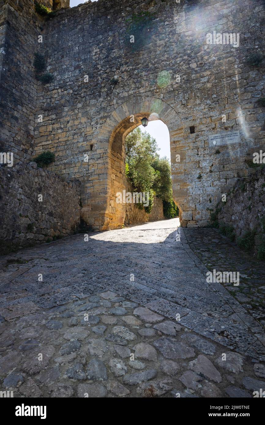 A cobble stone path through an arch in a stone wall with sunlight ...