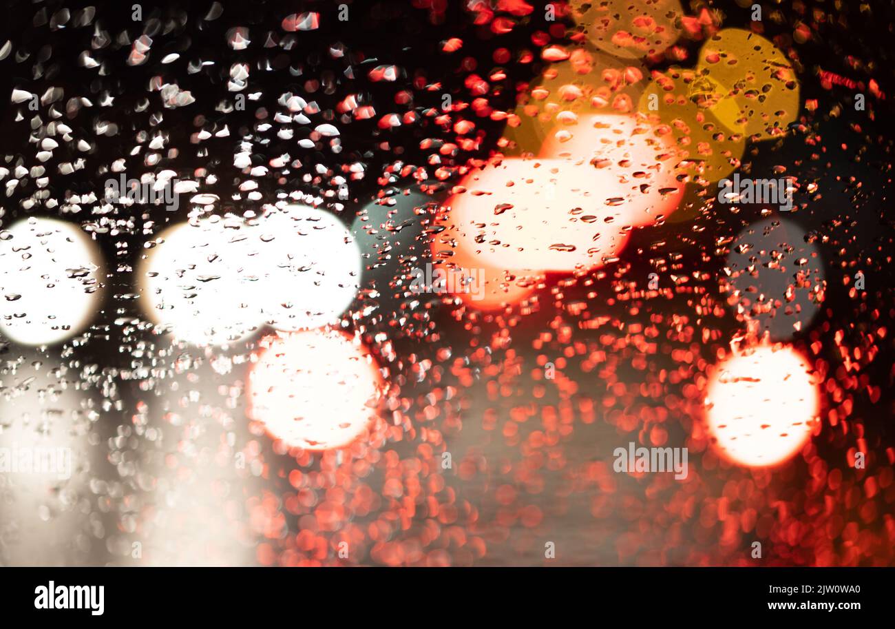 Blurred lights of cars at night behind the windshield with water drops ...