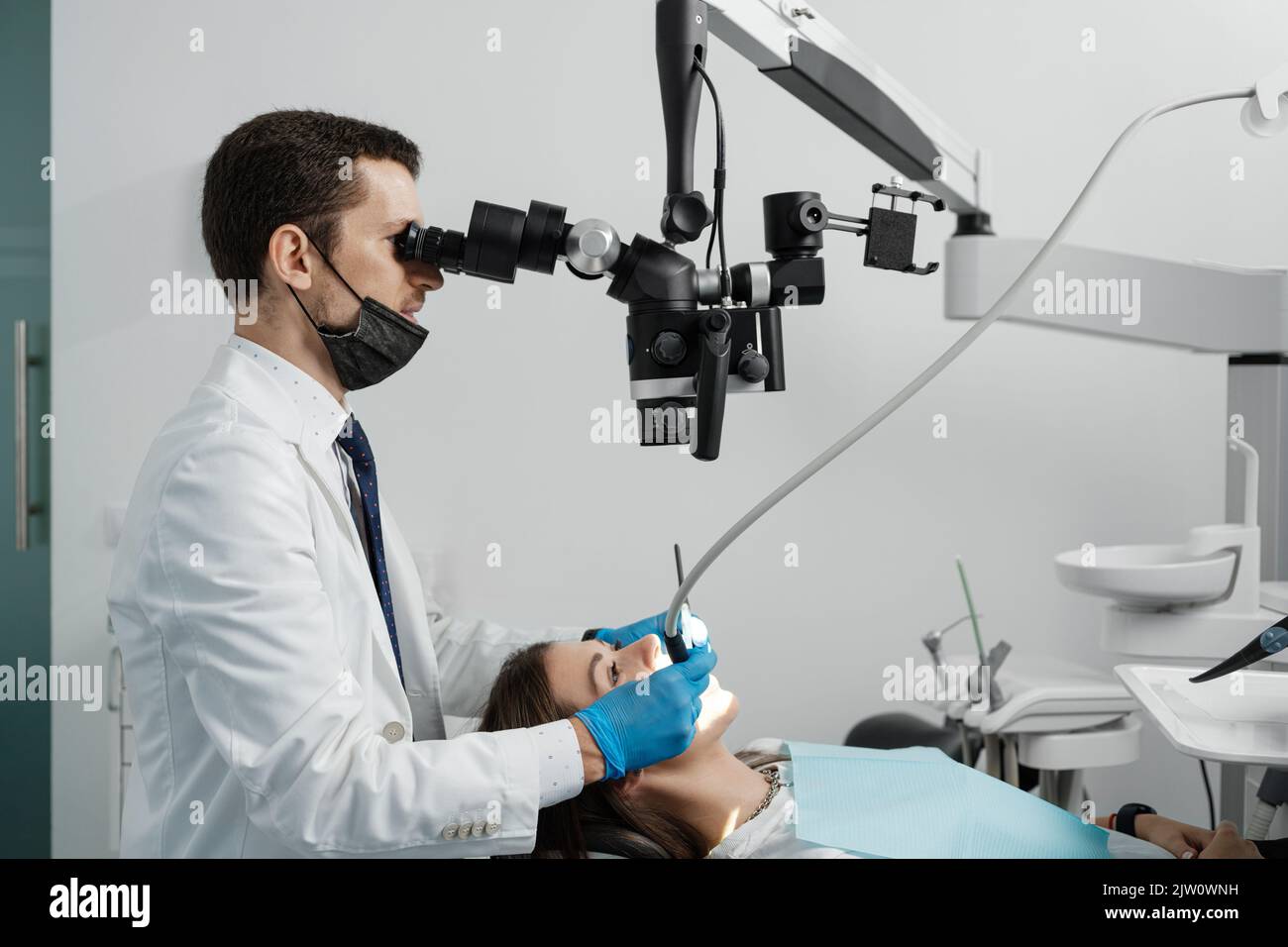 Male dentist using dental microscope treating female patient teeth at ...