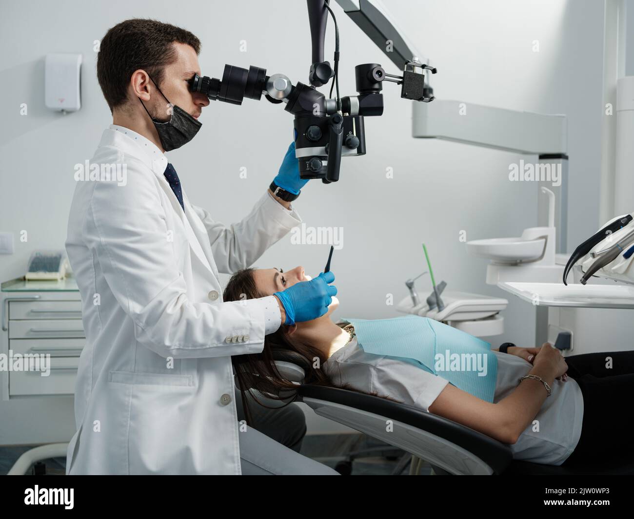 Male dentist using dental microscope treating female patient teeth at ...