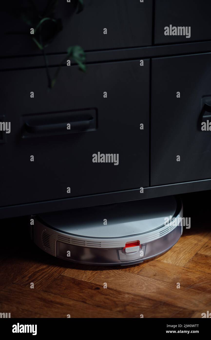 A vertical of a robot vacuum cleaner under a black cabinet Stock Photo ...
