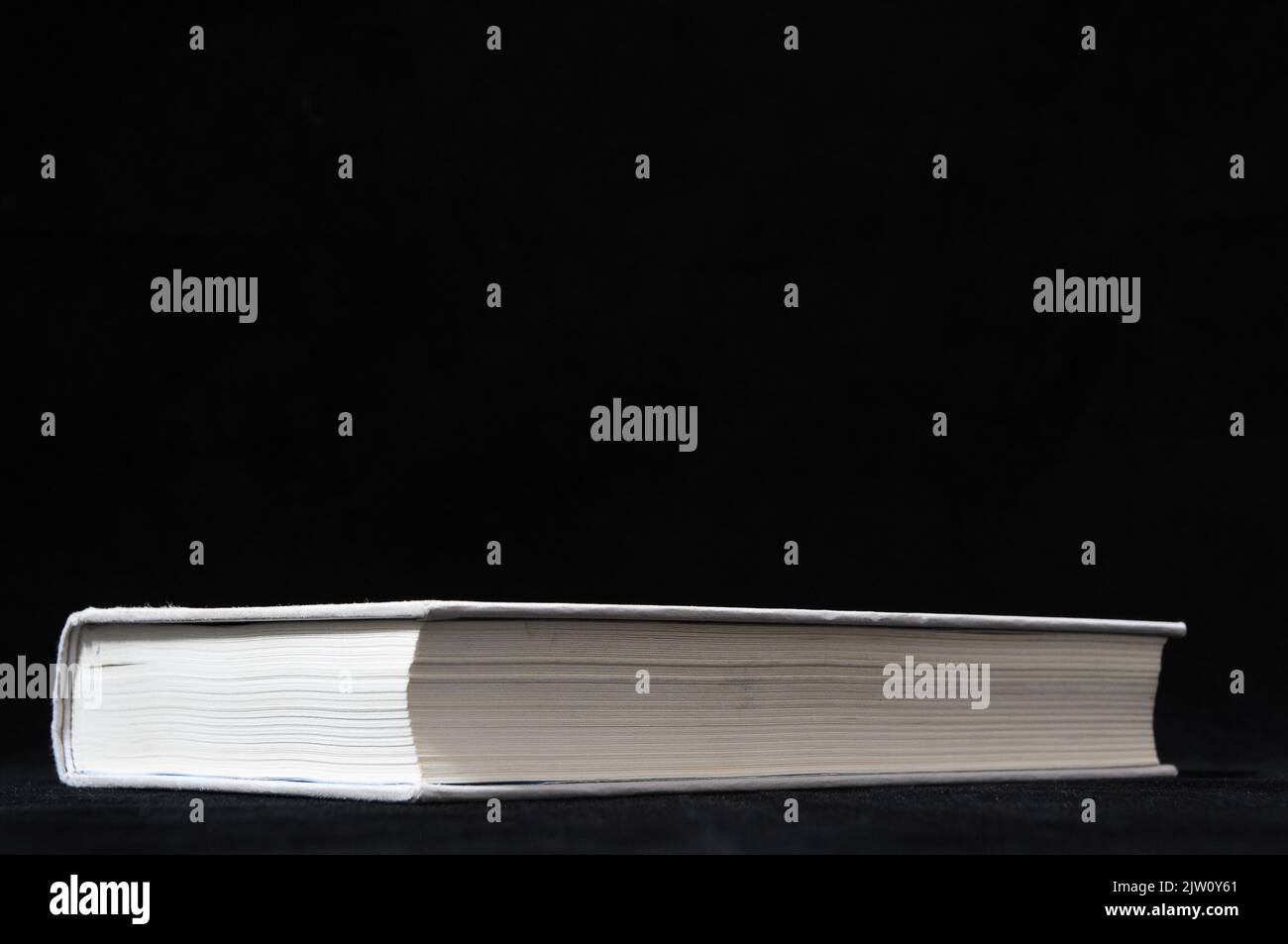 A white book laying flat on a surface in front of a black background ...