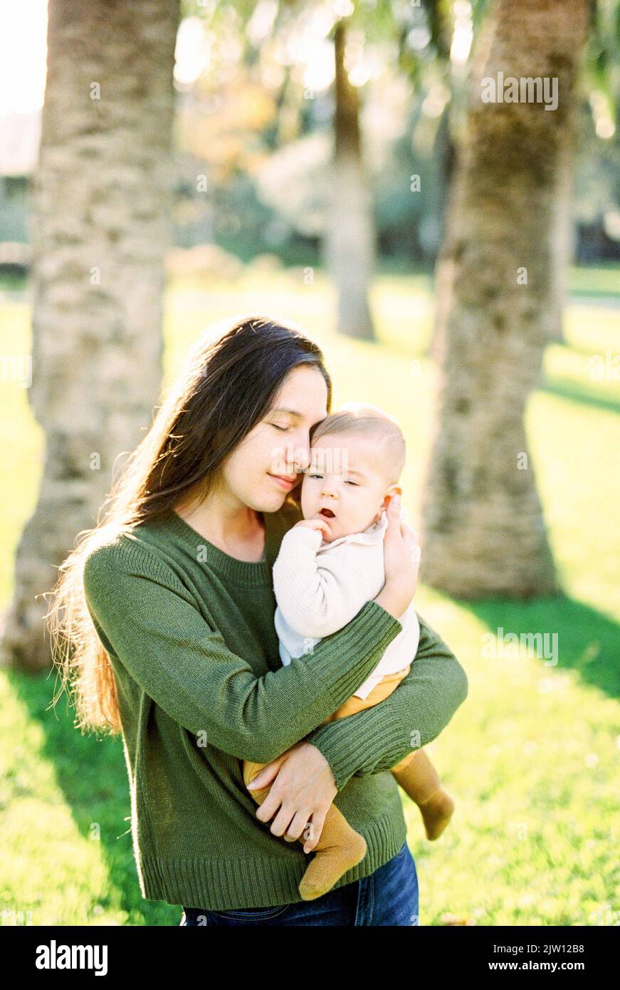 Mom hugs a sleepy baby in her arms, standing near palm trees Stock ...