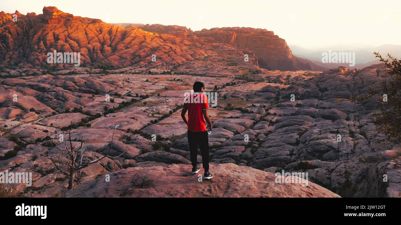 Rear view of man standing on edge of cliff with mountains in background ...