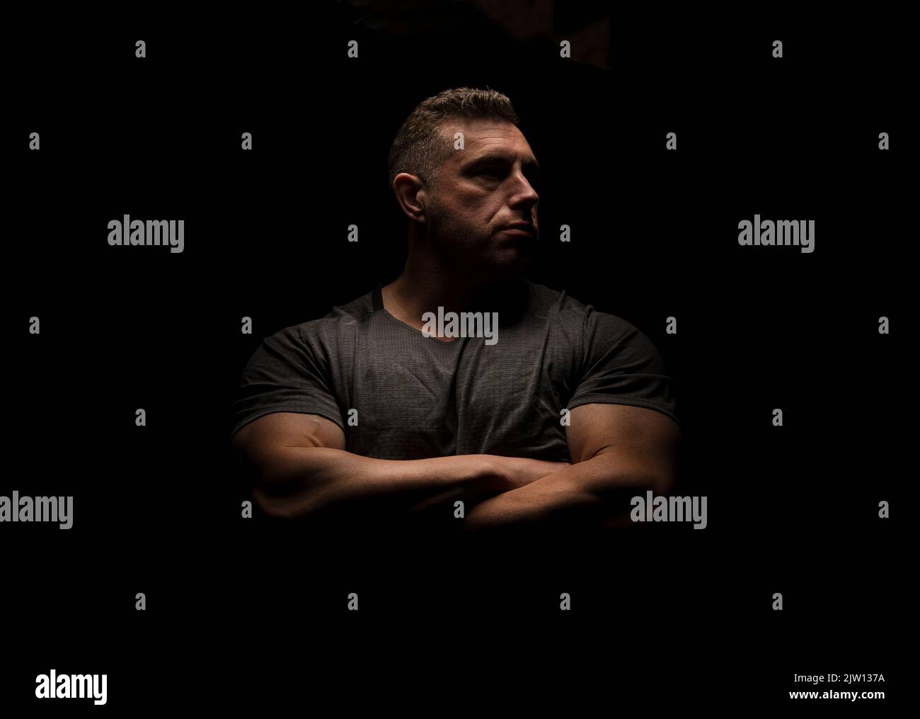 Large man folding his arms and looking away with top down lighting for ...