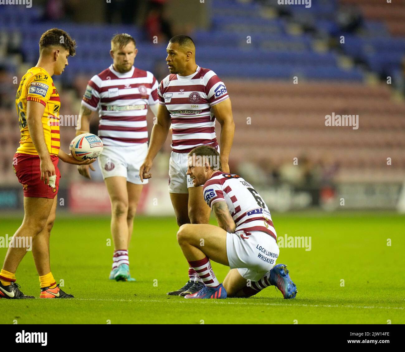 Cade Cust #6 of Wigan Warriors winces in pain as he holds his elbow ...