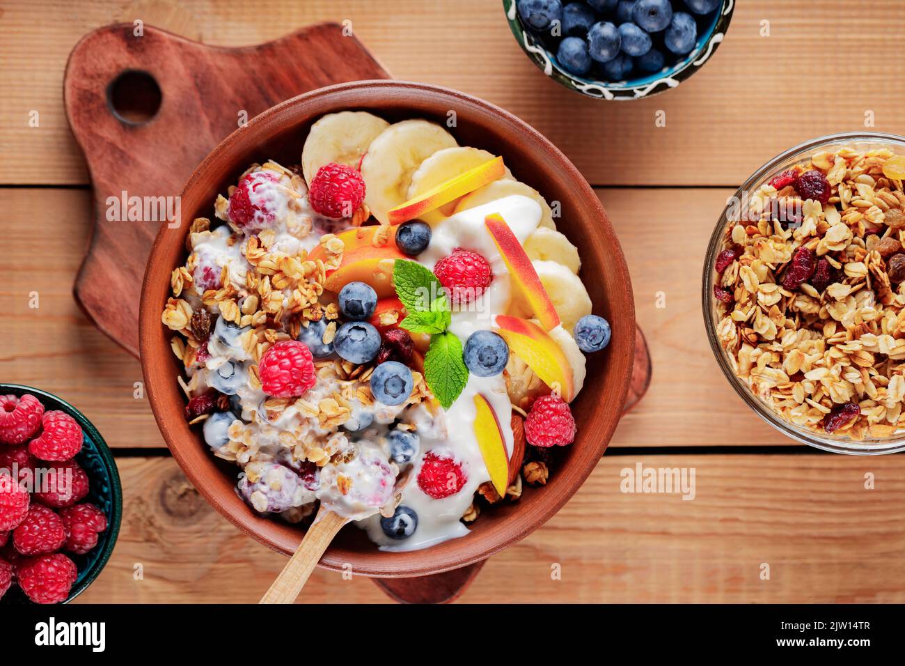 Yogurt with granola, fruits and berries on a clay plate with a wooden spoon. Yogurt with granola ...