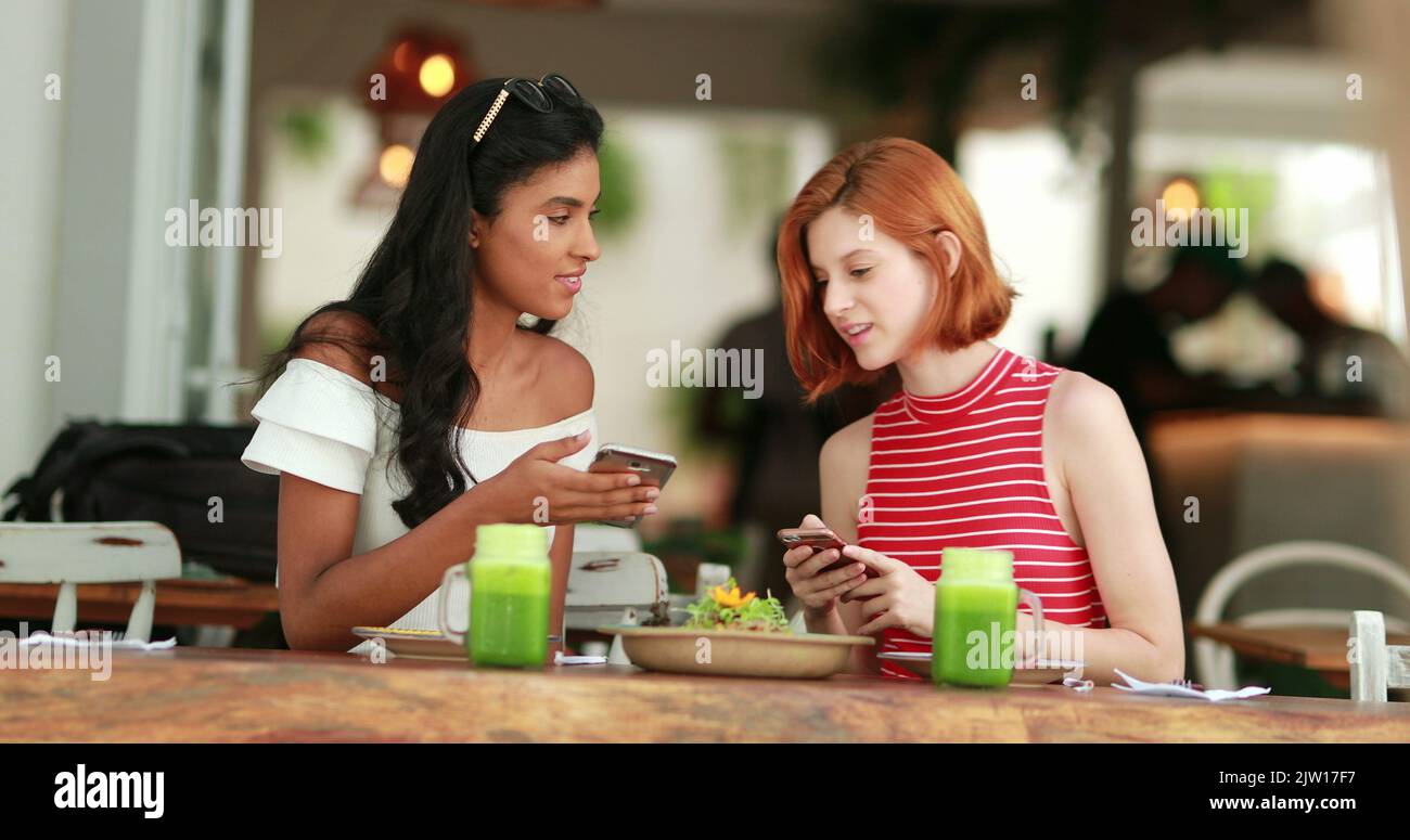 Attractive girls at restaurant, friend showing screen to female ...