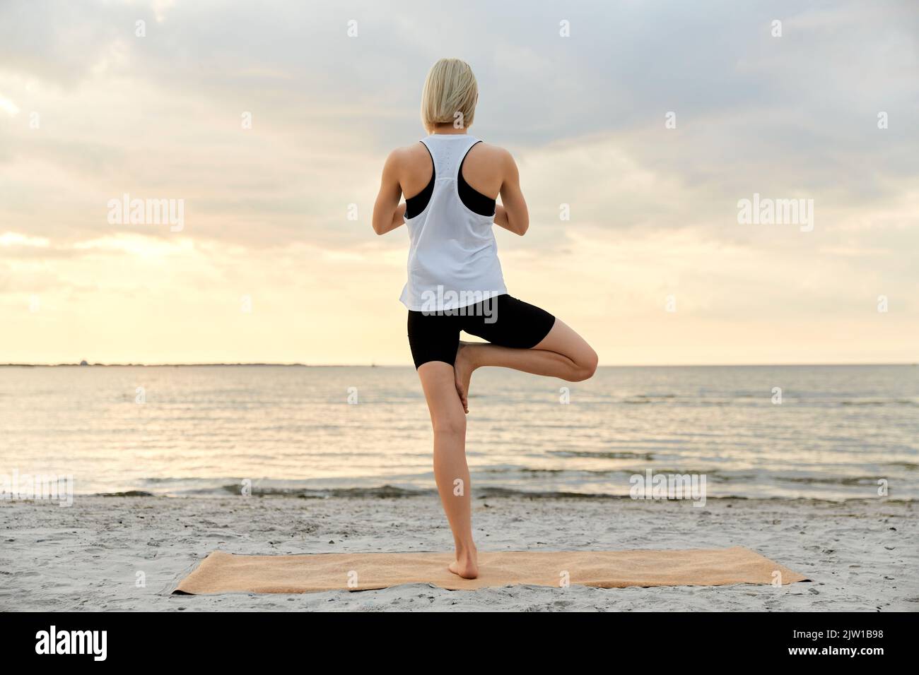 woman doing yoga tree pose on beach over sunset Stock Photo - Alamy