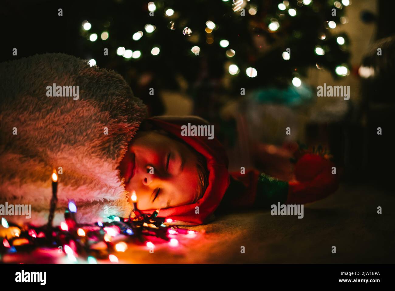 Boy child sleeps in cozy blanket and elf hat under christmas tree Stock ...