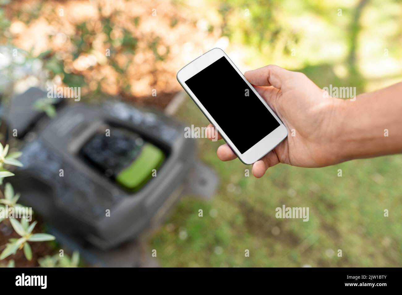 hand with smartphone and lawnmower at garden Stock Photo - Alamy