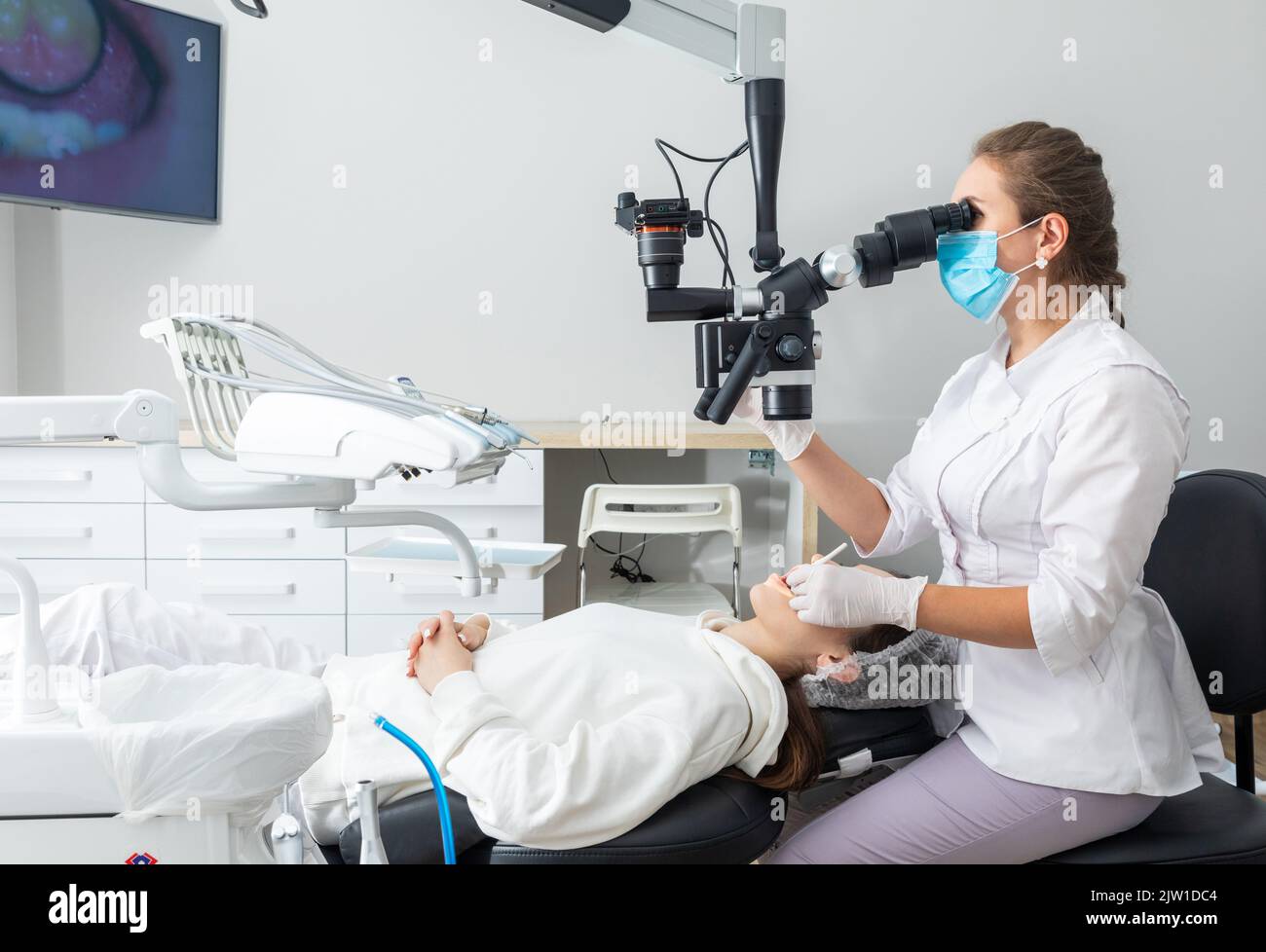 Female dentist using dental microscope treating patient teeth at dental ...