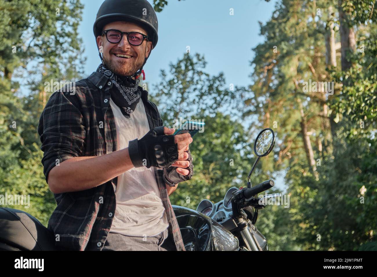 Young male biker in helmet using mobile phone and smiling sitting on a ...