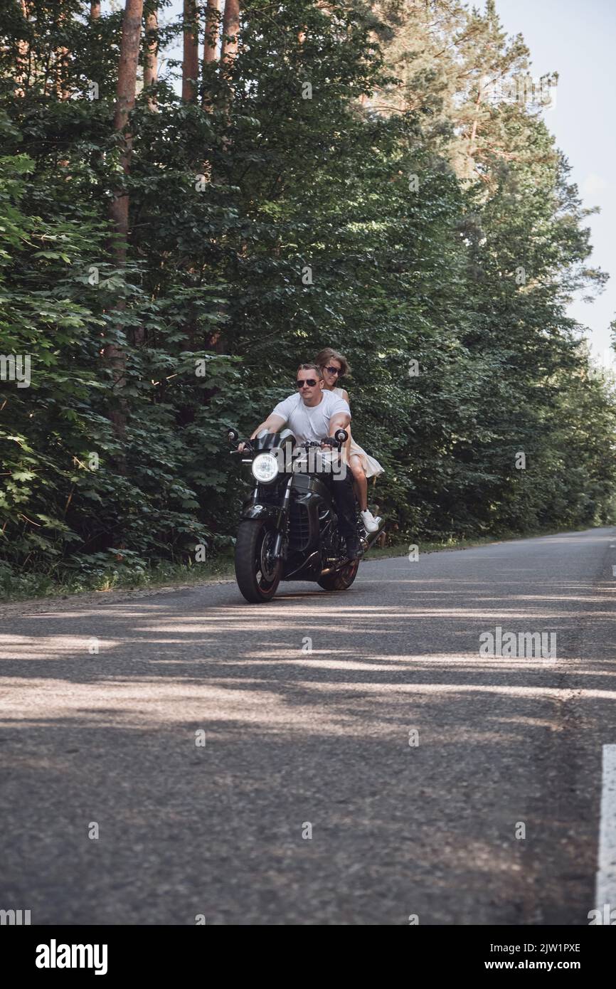 A young happy couple rides a motorcycle on an asphalt road in the ...