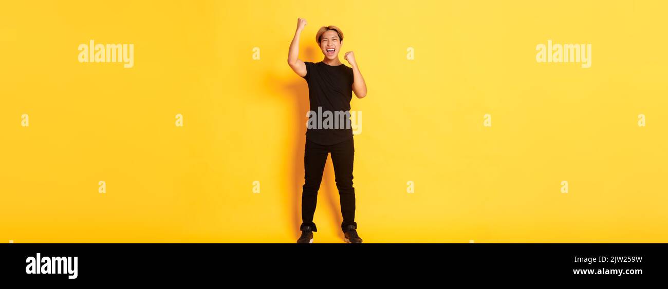 Full-length of triumphing handsome asian man with blond hair, raising ...