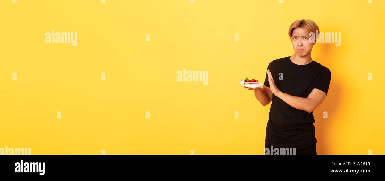Portrait of disgusted and upset young asian guy refuse eating cake ...