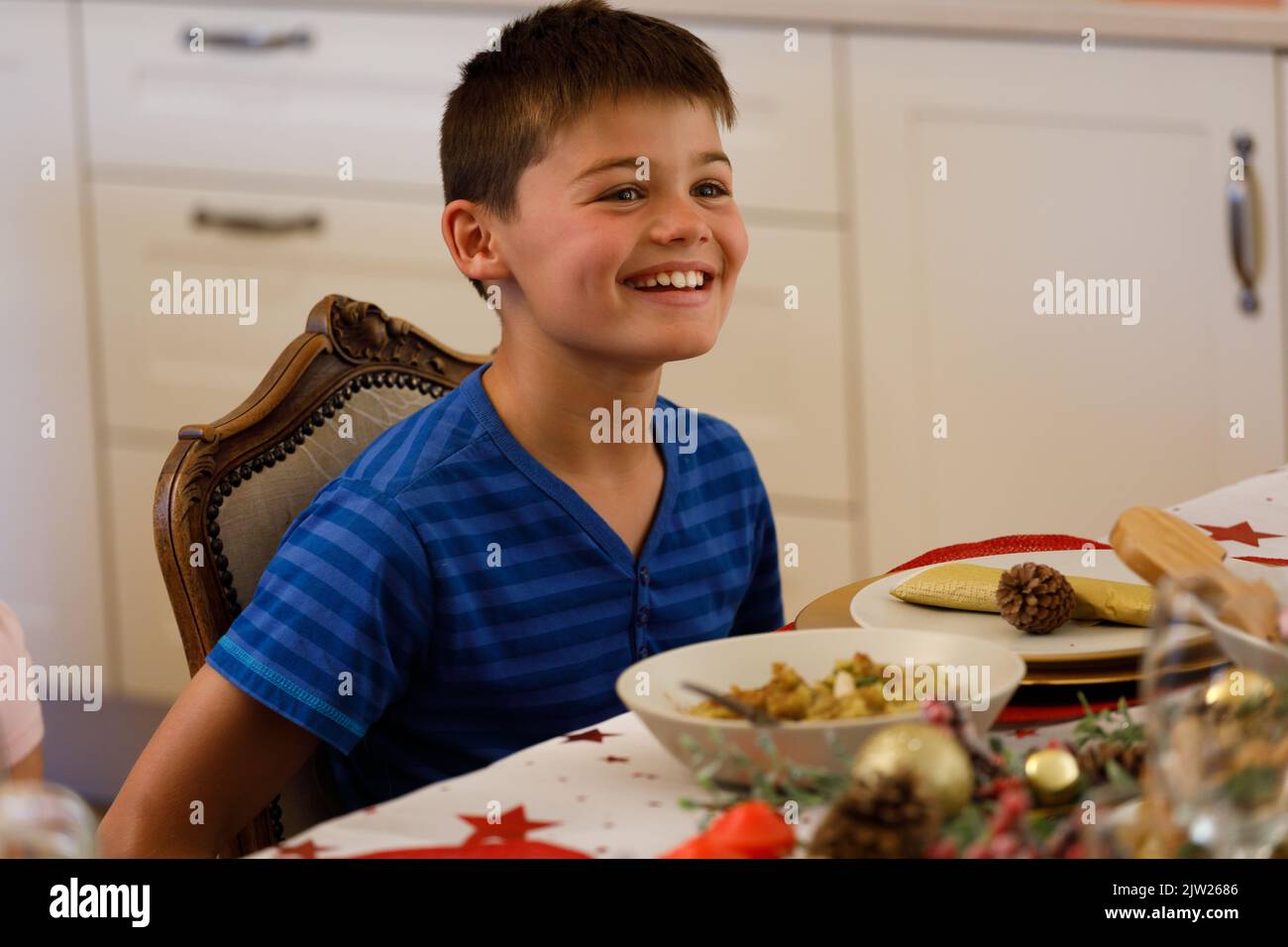 Caucasian boy sitting at table during dinner with family and smiling ...