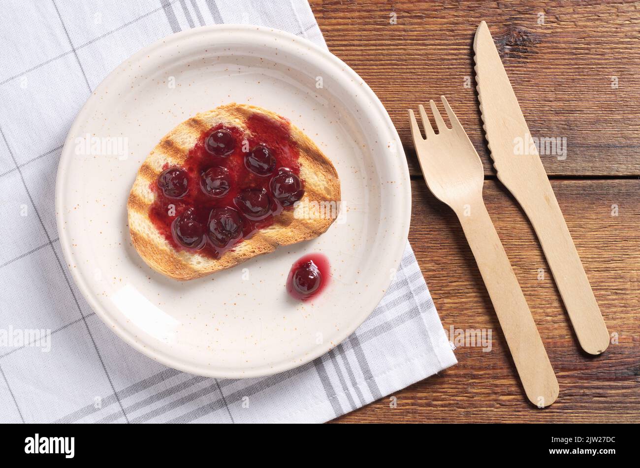 Grilled toasted bread with jam, wooden fork and knife on the table, top ...