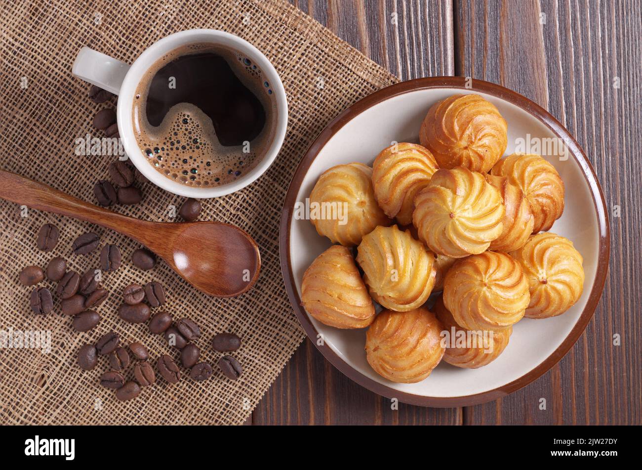 Small custard cakes in plate and cup of coffee on brown wooden table ...
