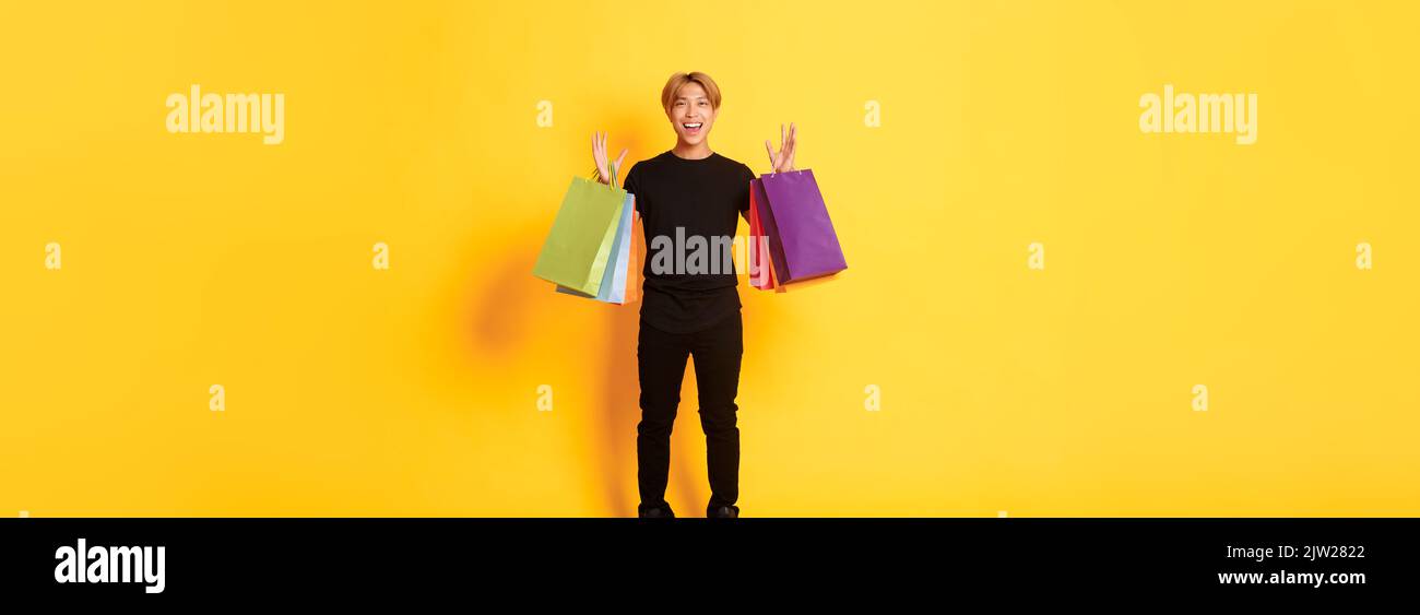 Full-length of happy handsome asian guy on shopping, holding bags and ...