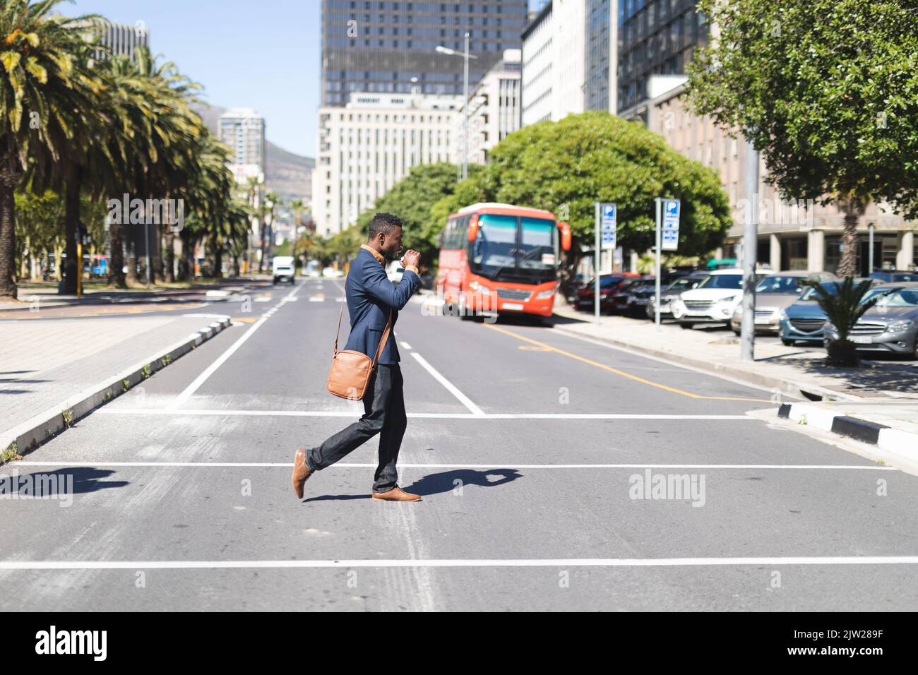 African american man crossing the road using smartphone and drinking ...
