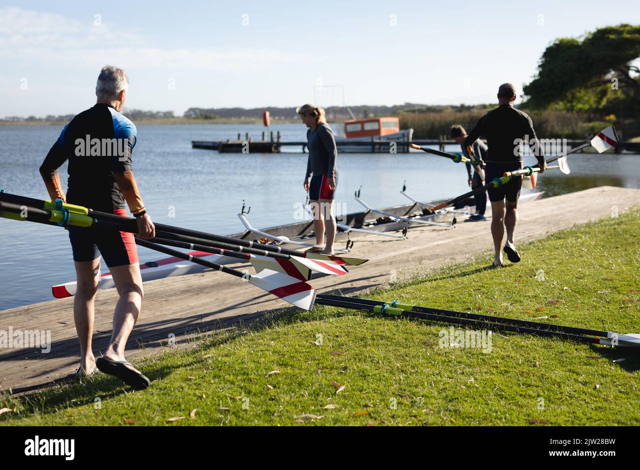 Senior caucasian rowing team carrying oars to the boat near the wooden ...