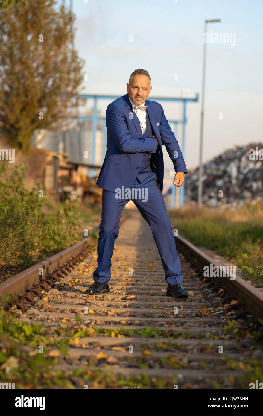 Mafia boss in blue suit on railway tracks, indicates to draw weapon ...