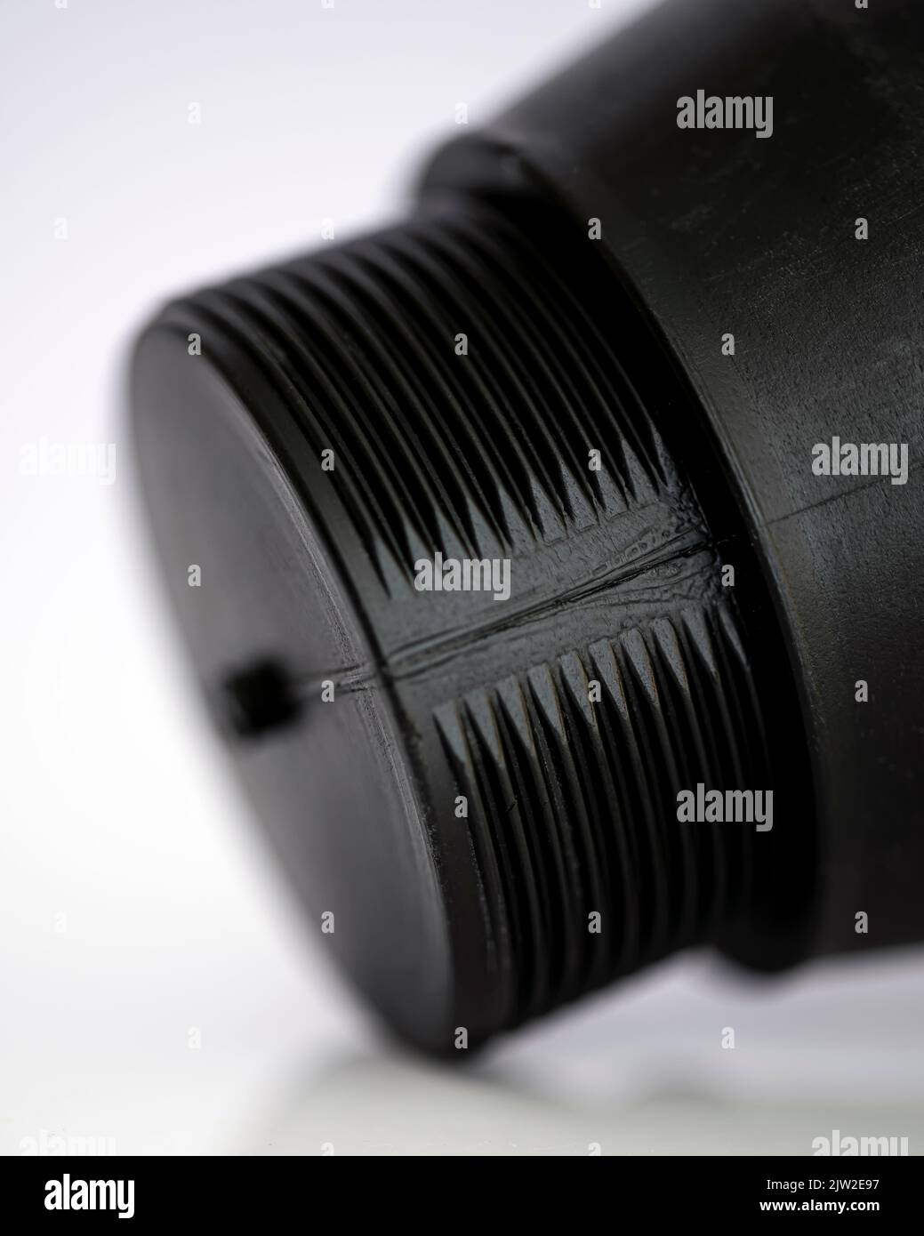 The end of a black plastic cylinder has a male thread, on a white ...
