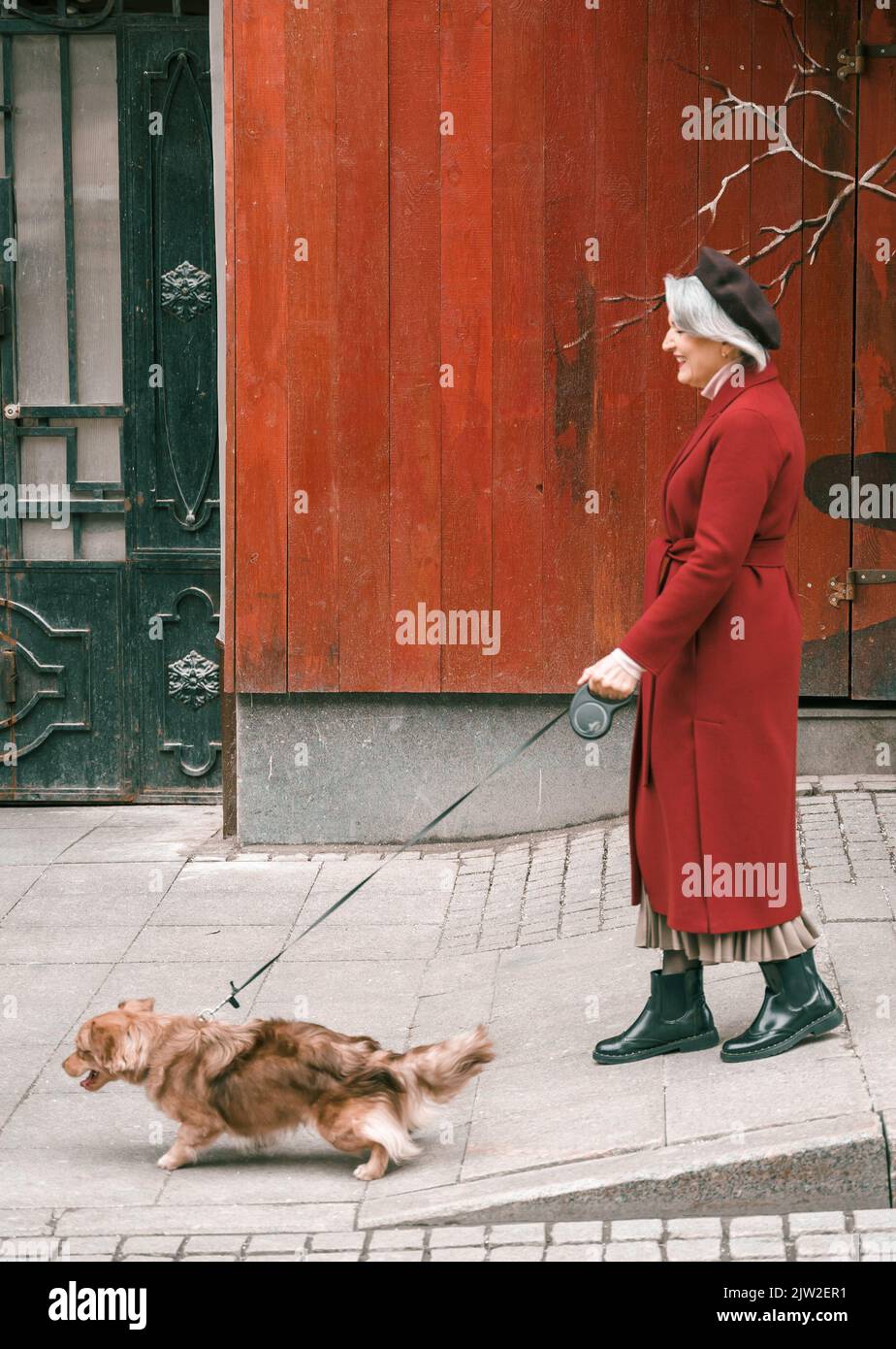 Elderly senior woman walking with lovely dog pet in red coat. Old ...