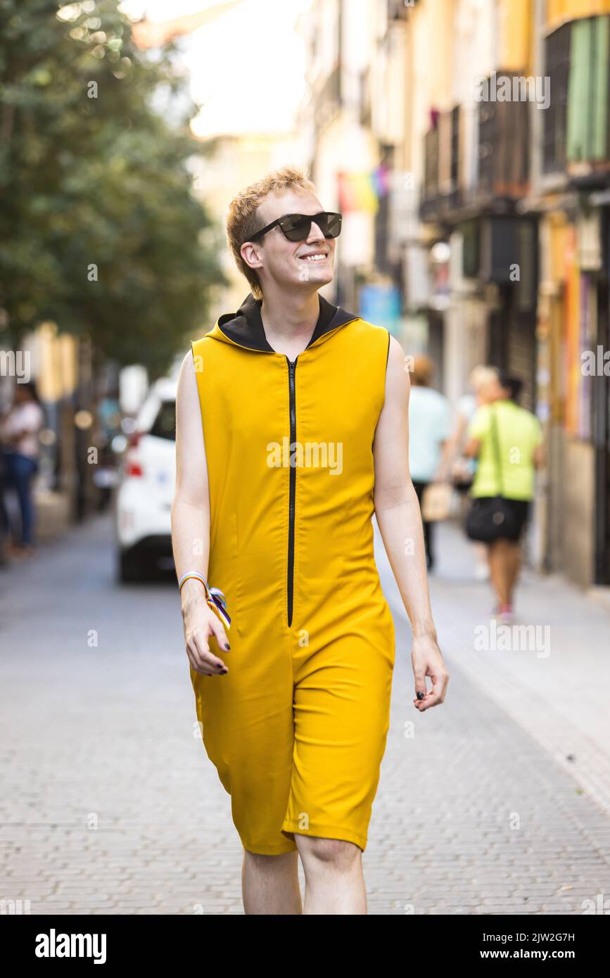 Cheerful transgender young man in yellow jumpsuit and sunglasses ...