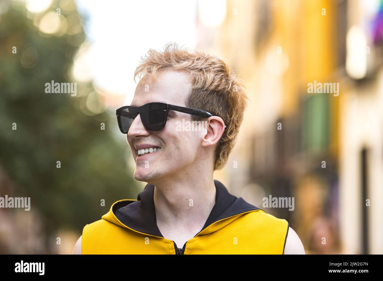 Cheerful transgender young man in yellow jumpsuit and sunglasses ...