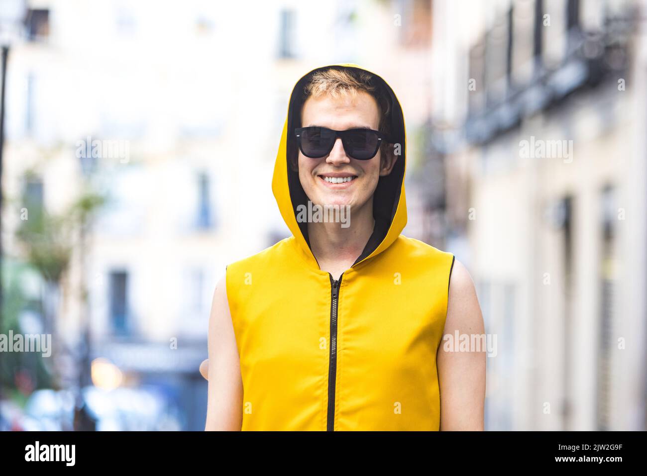 Cheerful transgender young man in yellow jumpsuit and sunglasses ...