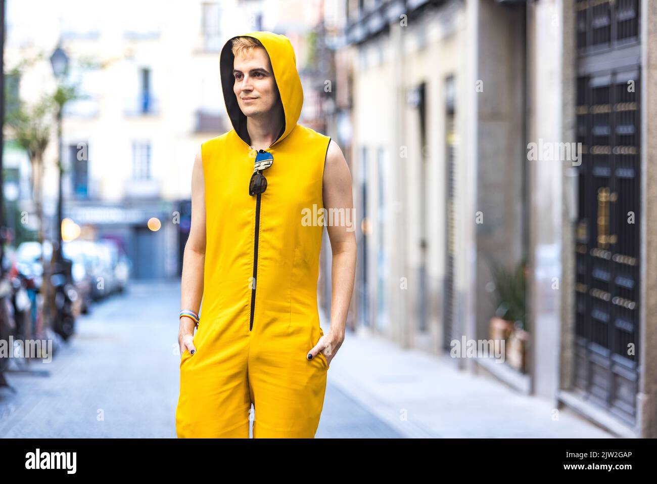 Happy transgender young man in yellow jumpsuit in hood looking away ...
