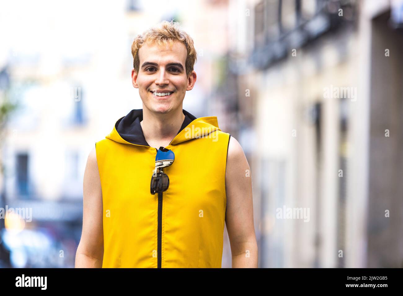 Cheerful transgender young man in yellow jumpsuit looking at camera ...