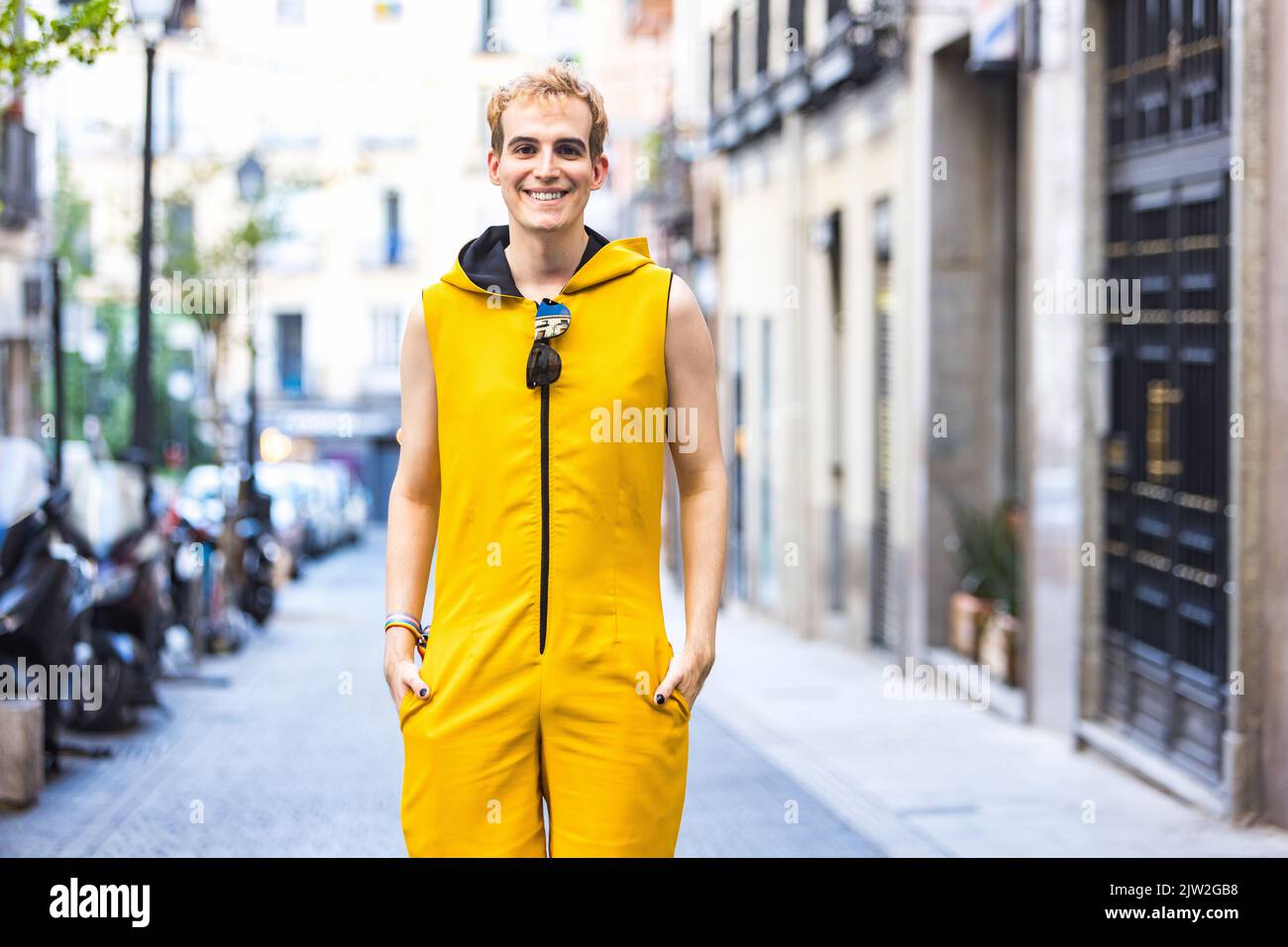 Cheerful transgender young man in yellow jumpsuit looking at camera ...