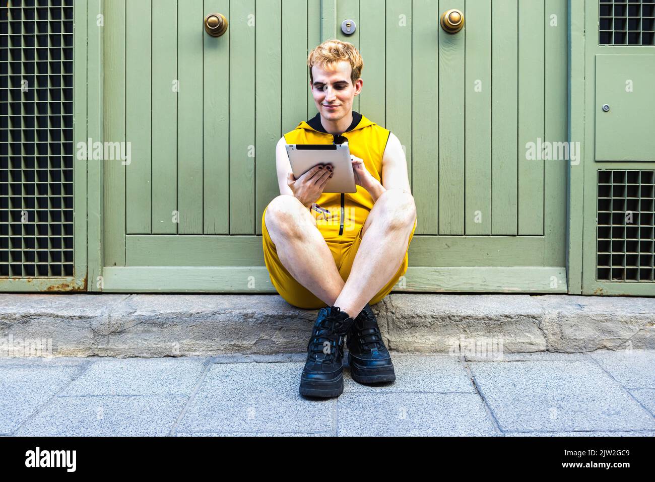 Young smiling transgender man in yellow jumpsuit browsing tablet while ...