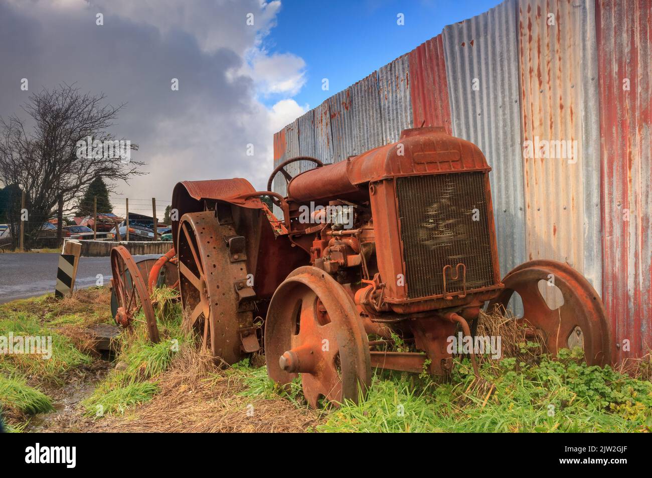 An old, rusted-out tractor beside a corrugated iron fence at a wrecker ...