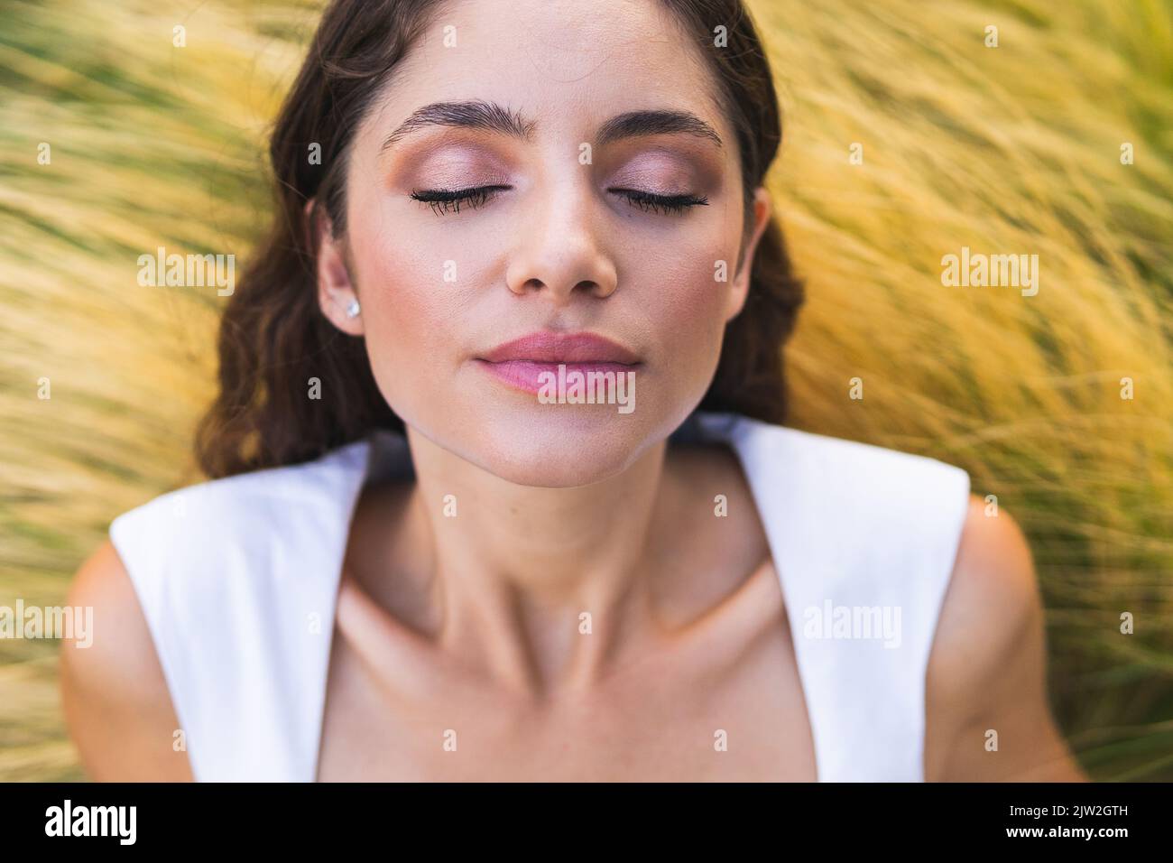 From Above Of Crop Graceful Female Model With Long Dark Hair And Makeup Lying On Grassy Lawn